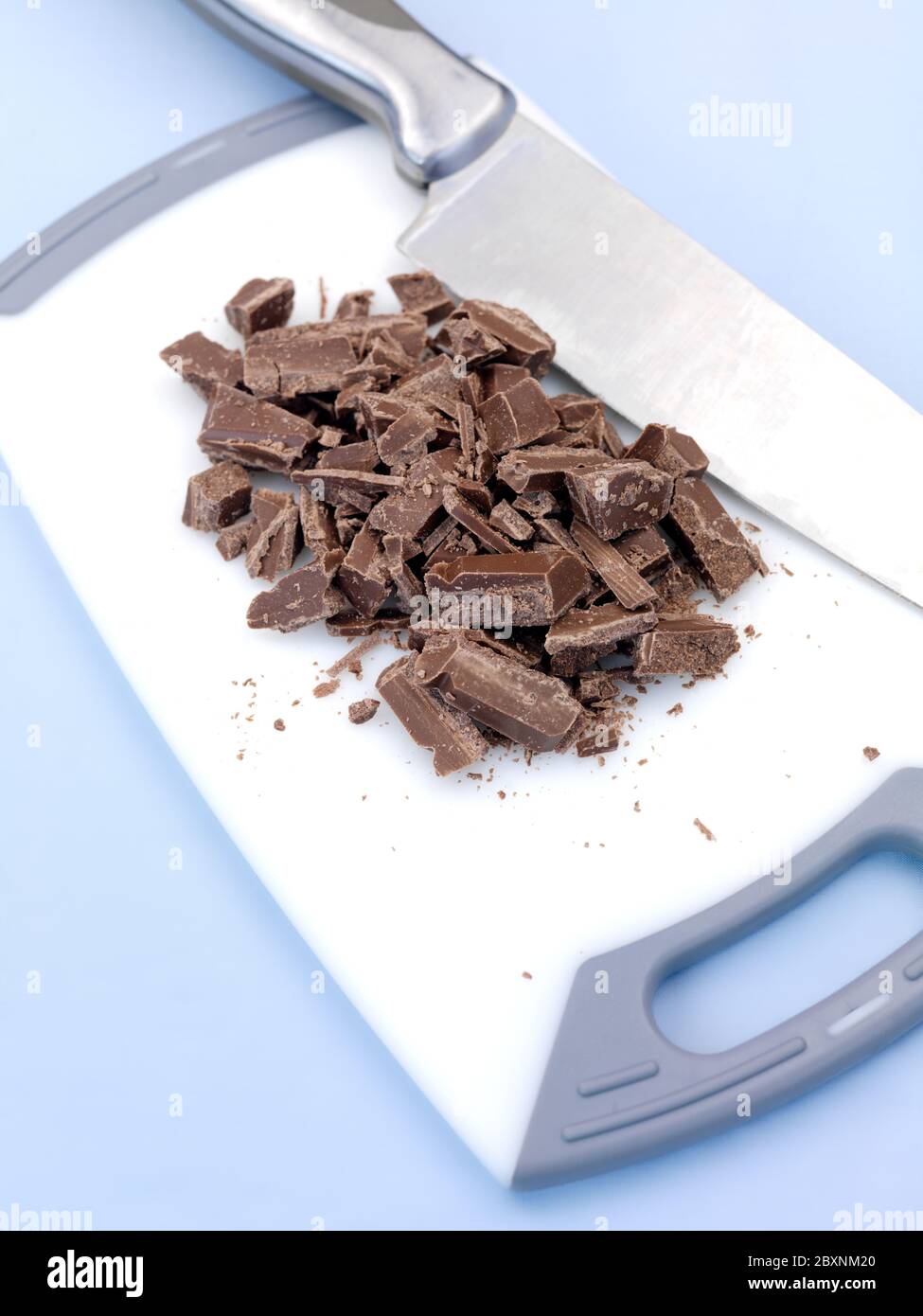 Cooking chocolate chopped on a cutting board isolated against a blue ...