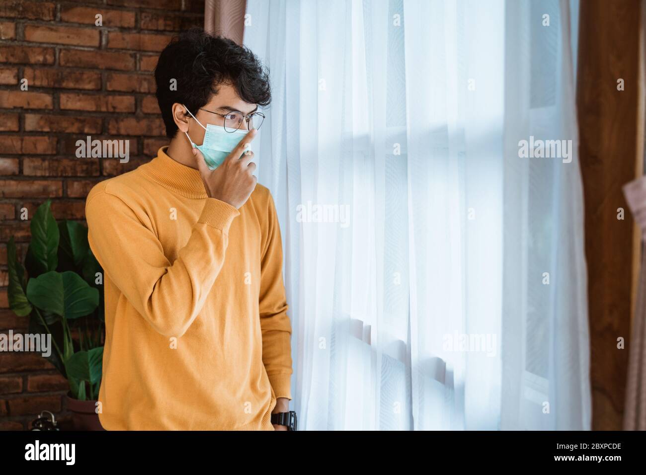 man wearing a mask looks sad when standing by the window Stock Photo ...