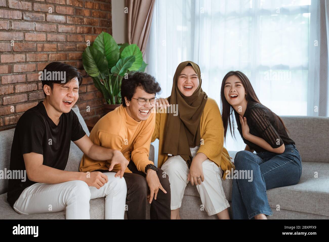 group of Asian young people sitting together on the couch laughing ...