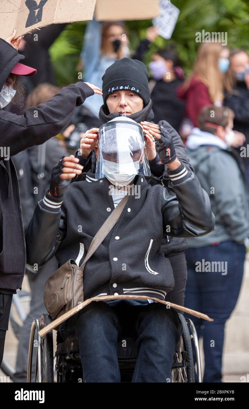 Man, in a wheelchair, is helped on with his protective face shield at ...