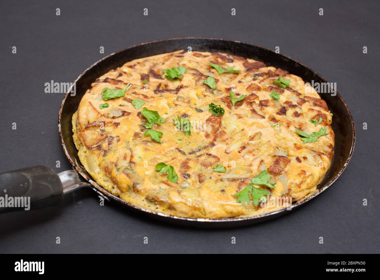 A Libyan potato omelette photographed against a black studio background ...