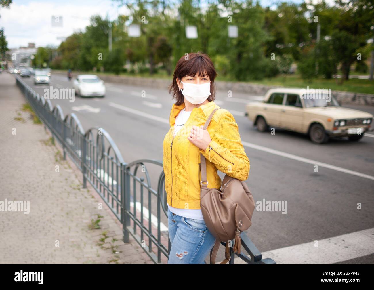 Adult pretty woman in casual clothes and bag with a protective mask on ...