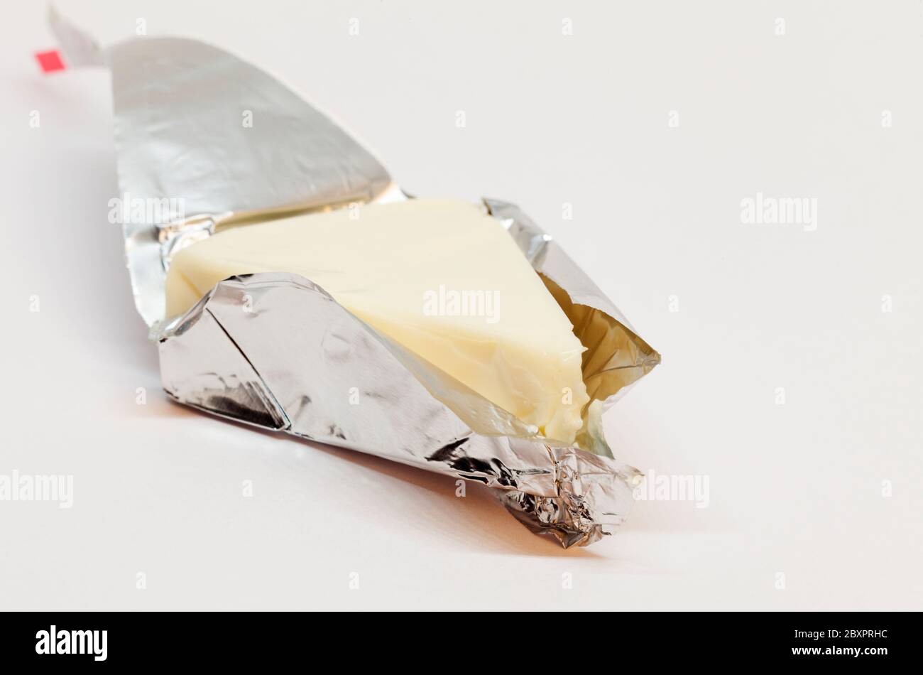 a triangular cheese wrapped in silver foil on white background Stock ...