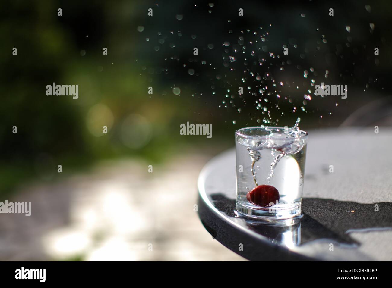 Red cherry falling into a glass of water producing water splash, freeze ...