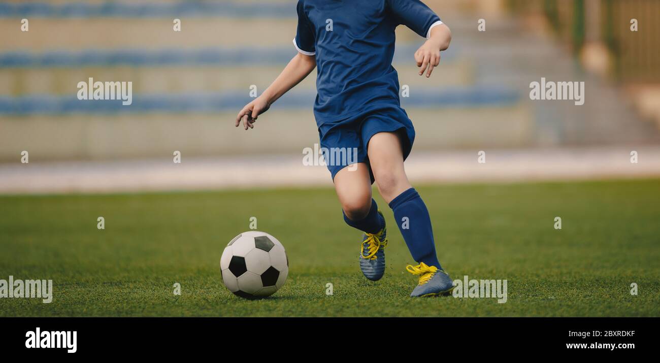 Junior level football player running with a ball. Footballer in soccer ...