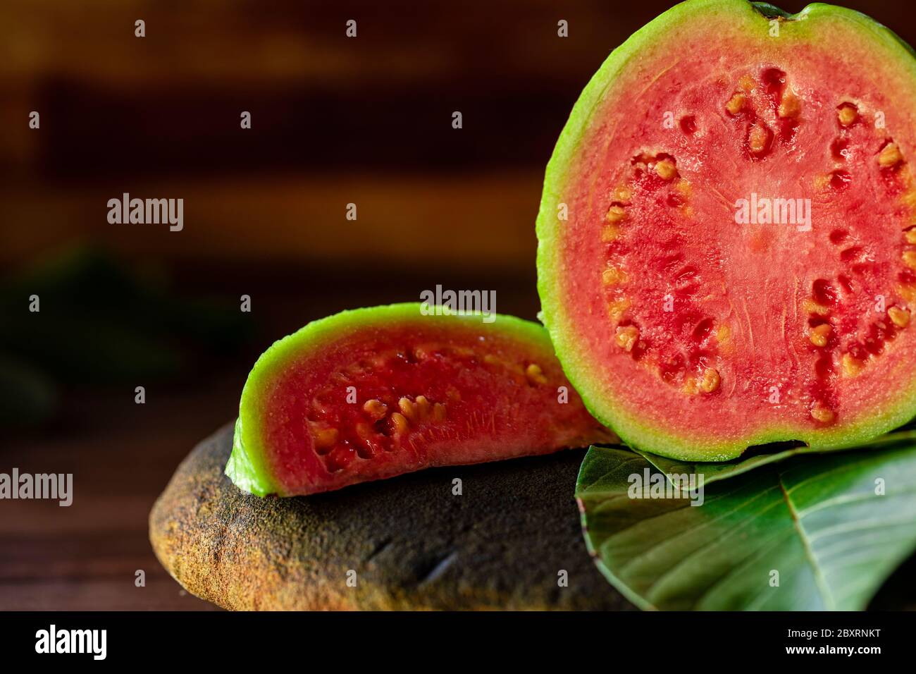 Fresh red guavas with green leaves on wooden demolition background ...