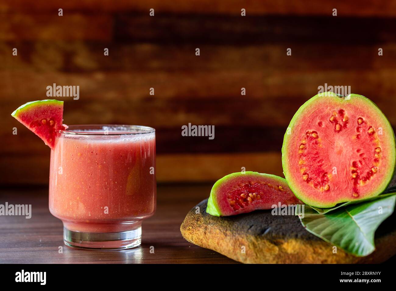 Delicious red guava juice alongside a slice of guava, in the background ...