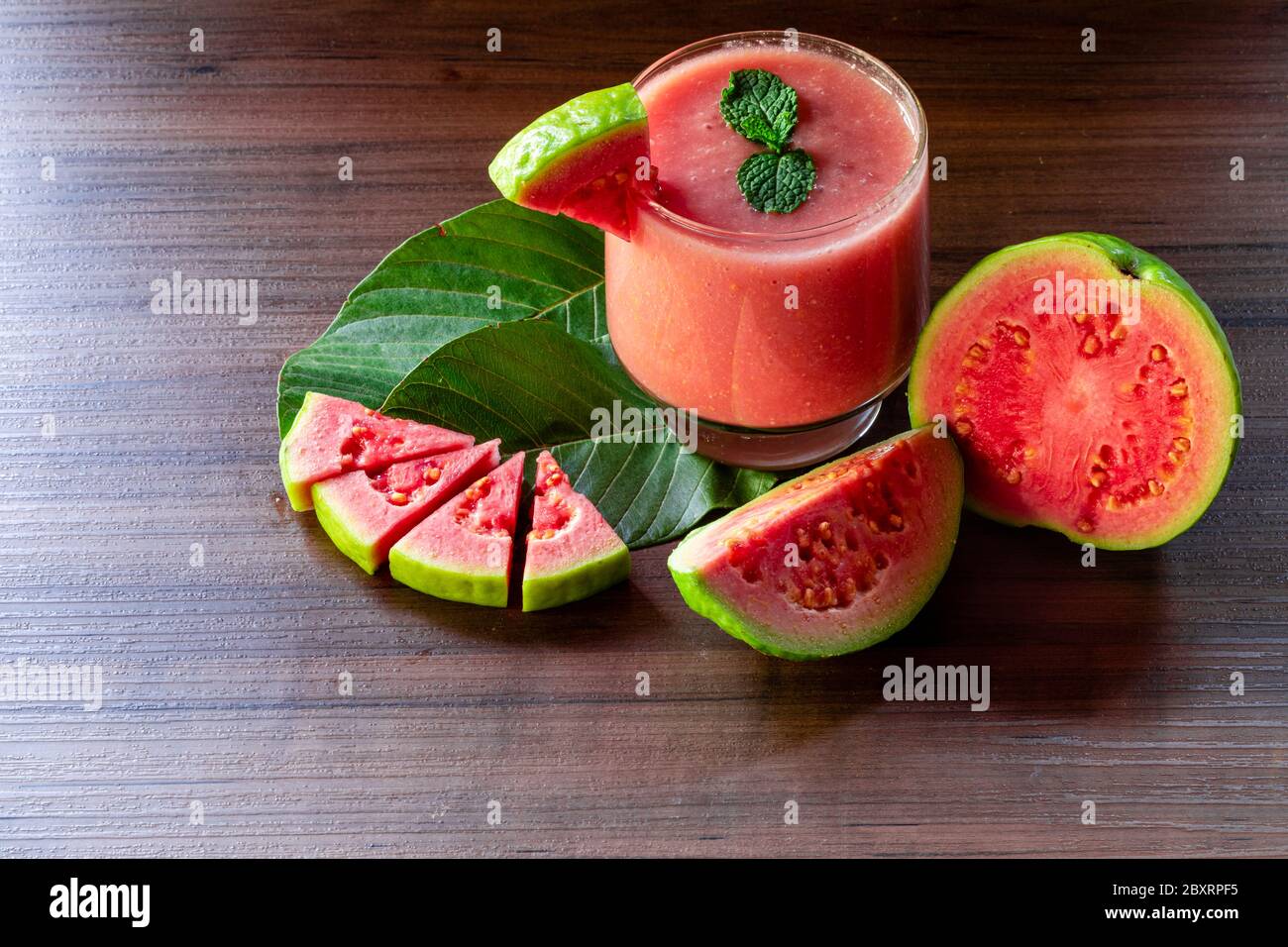 Delicious red guava juice alongside a slice of guava, in the background ...