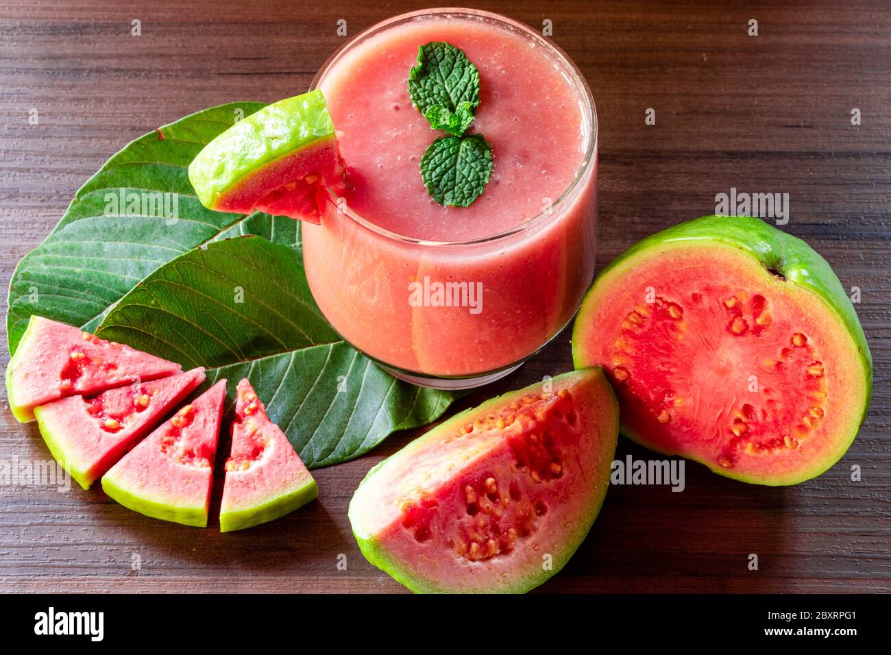 Delicious red guava juice alongside a slice of guava, in the background ...