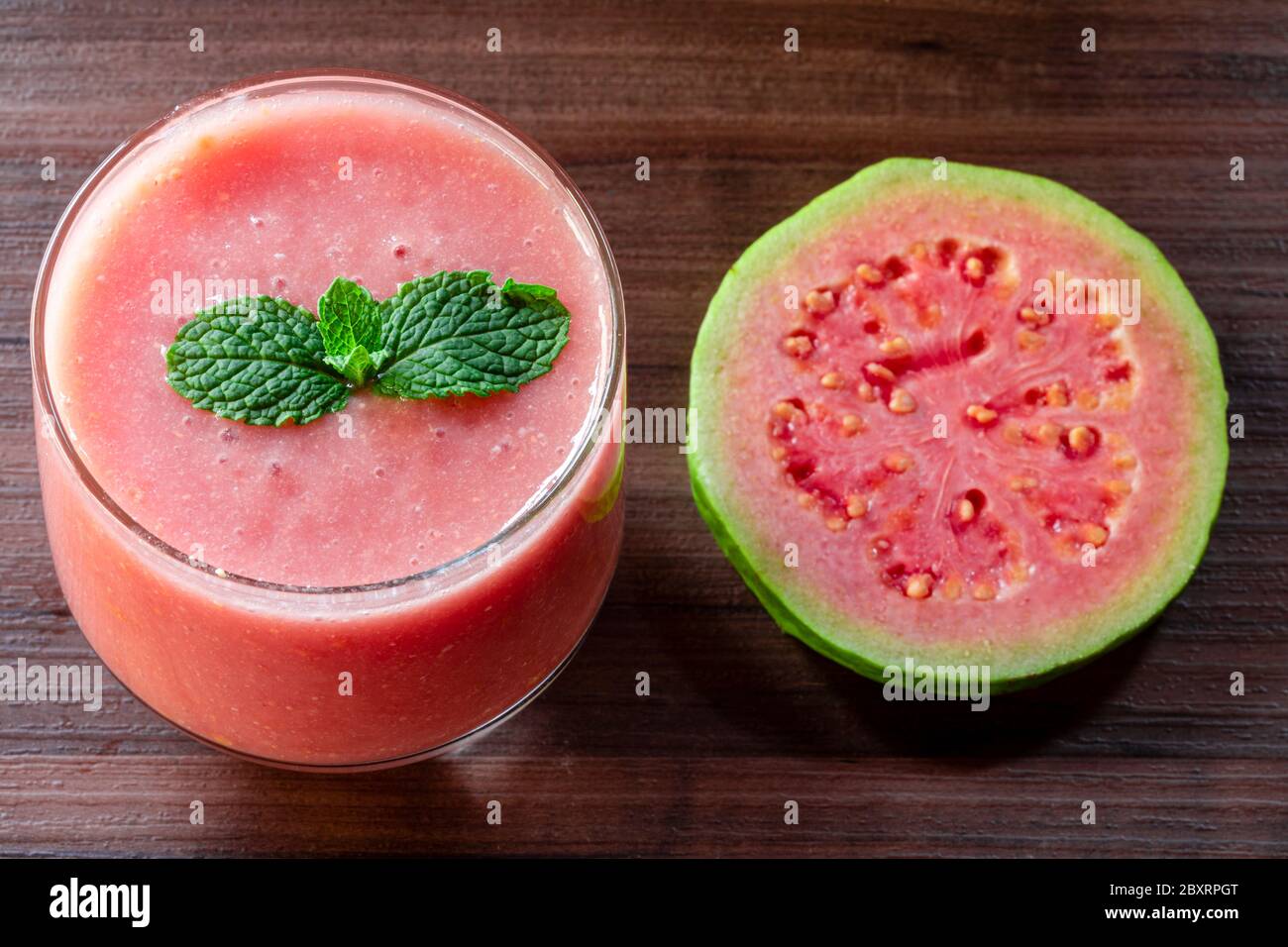 Delicious red guava juice alongside a slice of guava, in the background ...