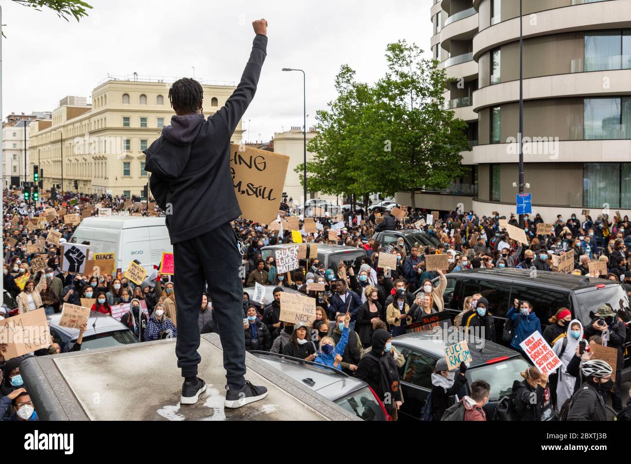 A black man stands on top of a bus stop with his fist raised above a ...