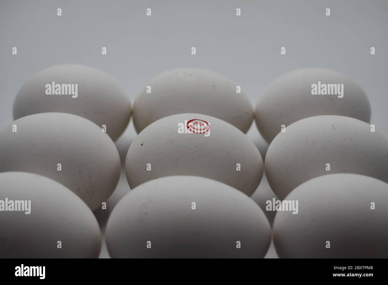 Close up of isolated white raw egg with painting of red smiling face ...