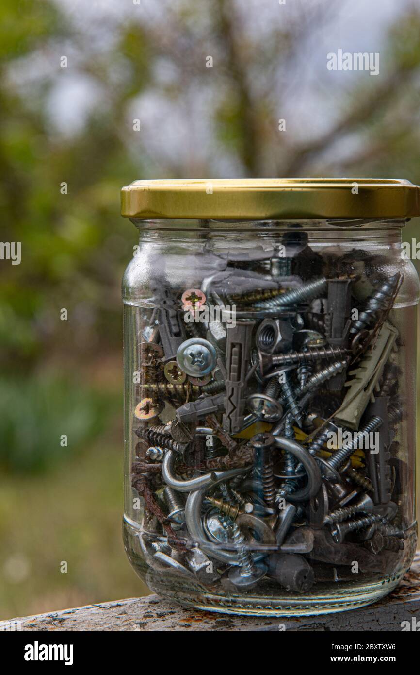 Glass jar of assorted hardware bolts and nuts closeup through blurry ...