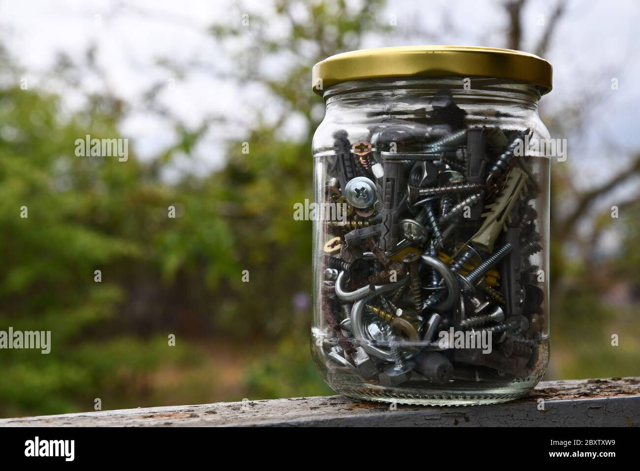 Old glass jar of assorted hardware bolts and nuts inside through blurry ...