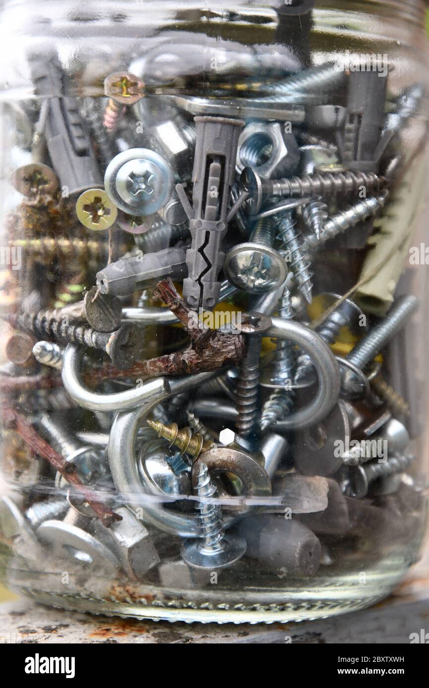 Photo shot through blurry thin glass jar with old metal bolts and nuts ...