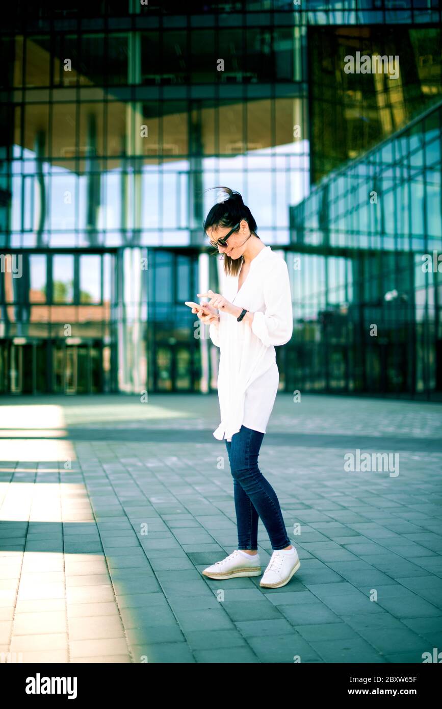 Full length shot of happy woman text messaging while standing outdoor ...