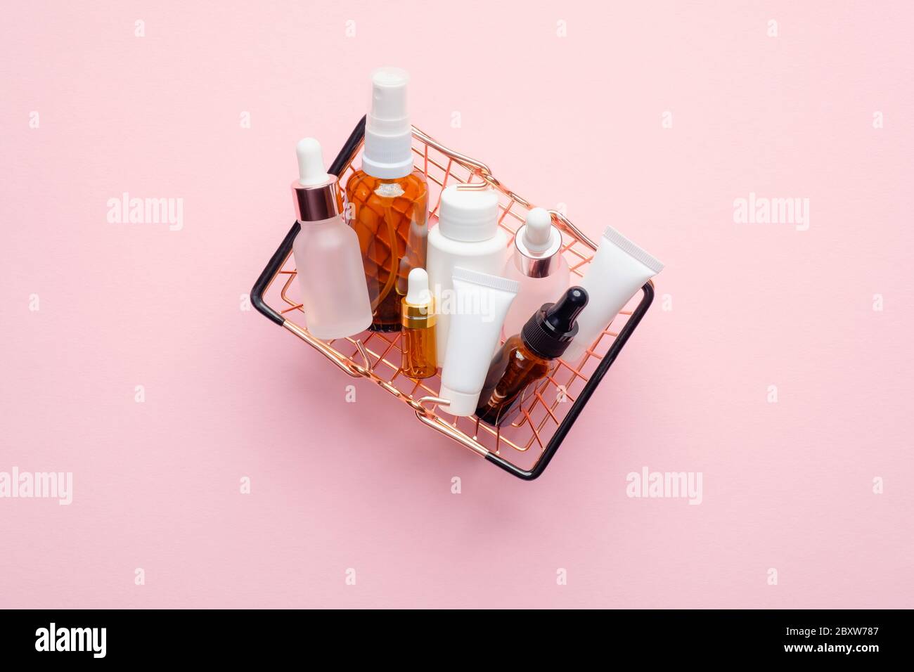 Shopping basket full of cosmetic bottles and packaging on pink ...