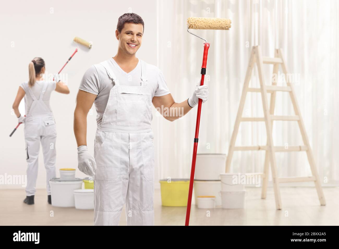 Male painter with a paint roller posing and a female painter painting a ...