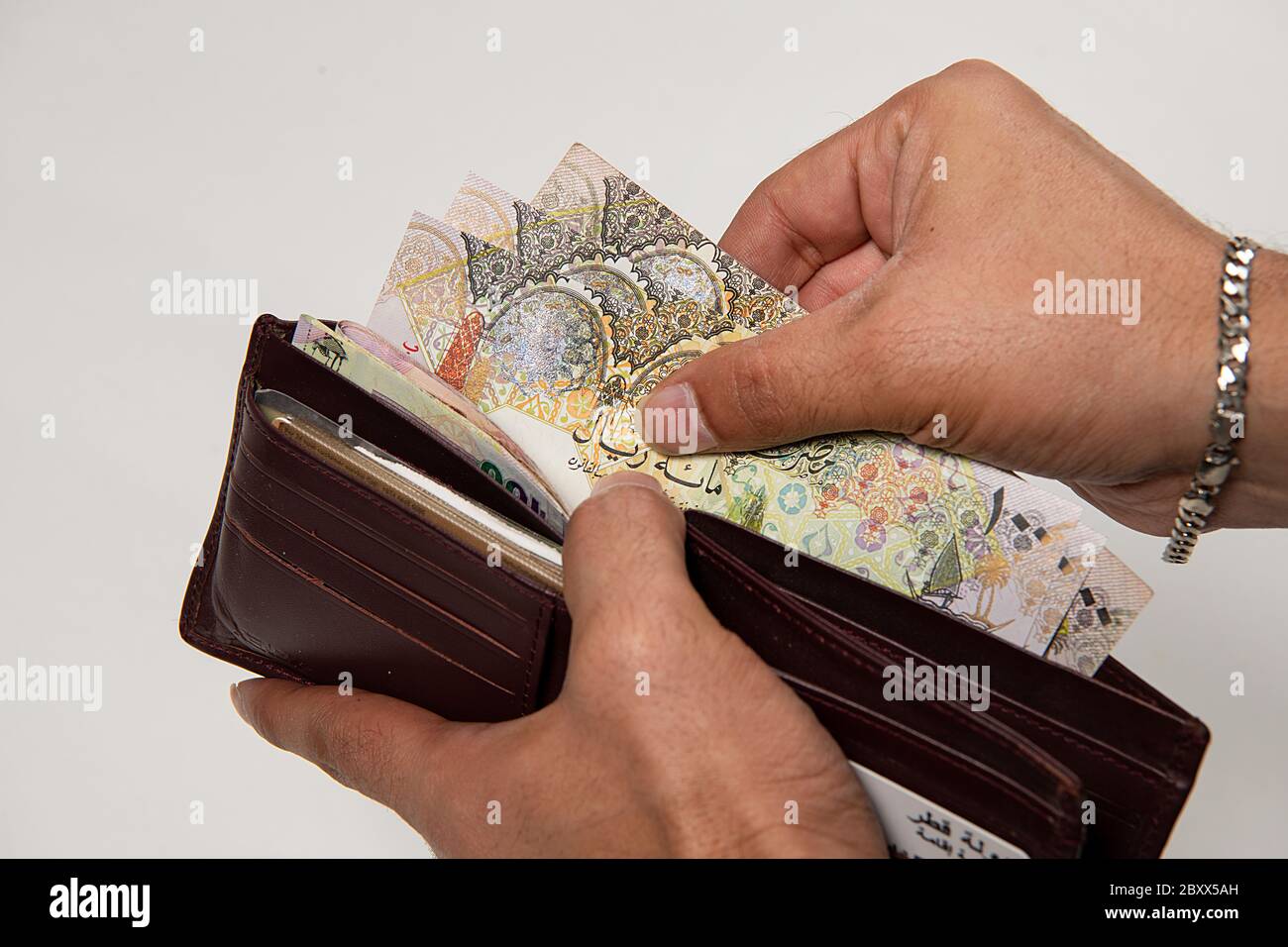 Men's hands holding wallet with Qatari notes. 100 Rial new notes ...