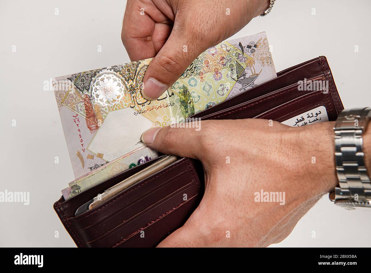 Men's hands holding wallet with Qatari notes. 100 Rial new notes ...