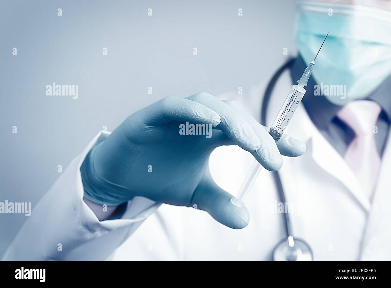 Doctor in gauze mask and medical robe holding syringe in his blue ...