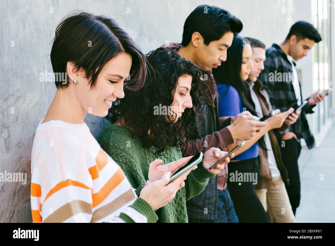 Group of young adults stare at their cell phones while standing against ...