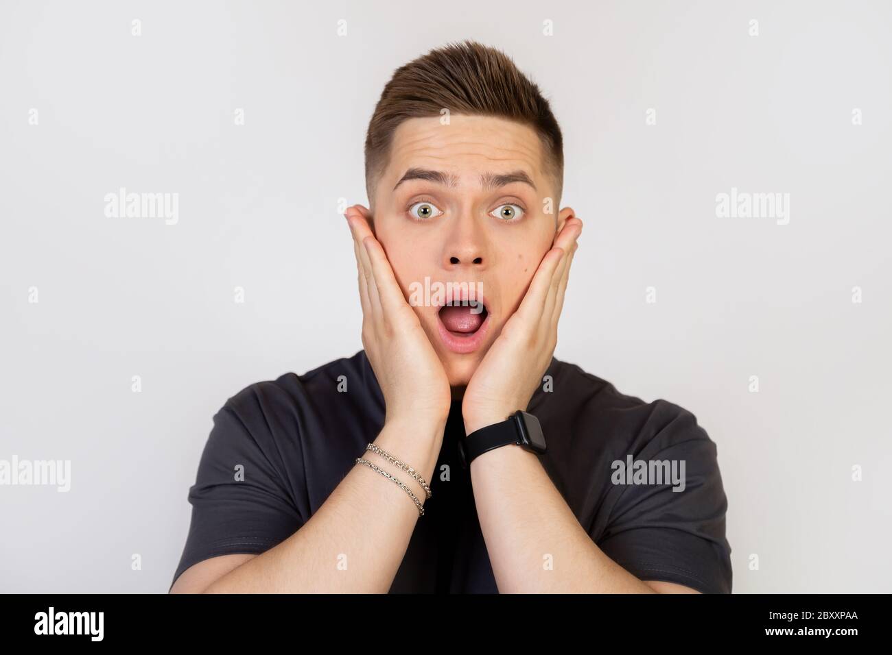 Shocked young man holding his hands on his cheeks, looking with ... Shocked young man holding his hands on his cheeks, looking with ...