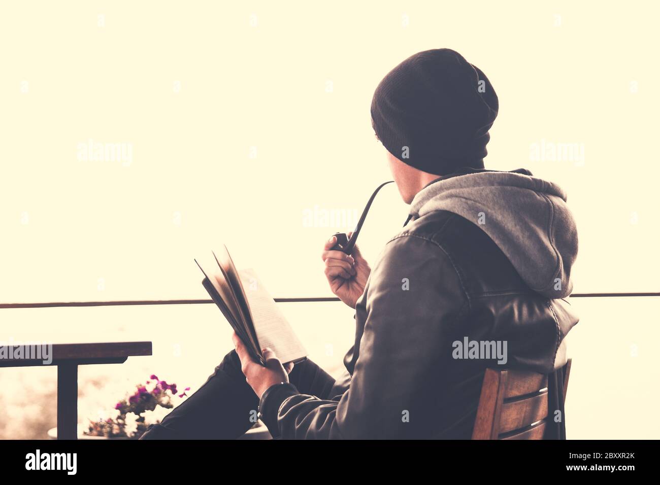 Back view on young black haired man witn piercing reeding a book and ...