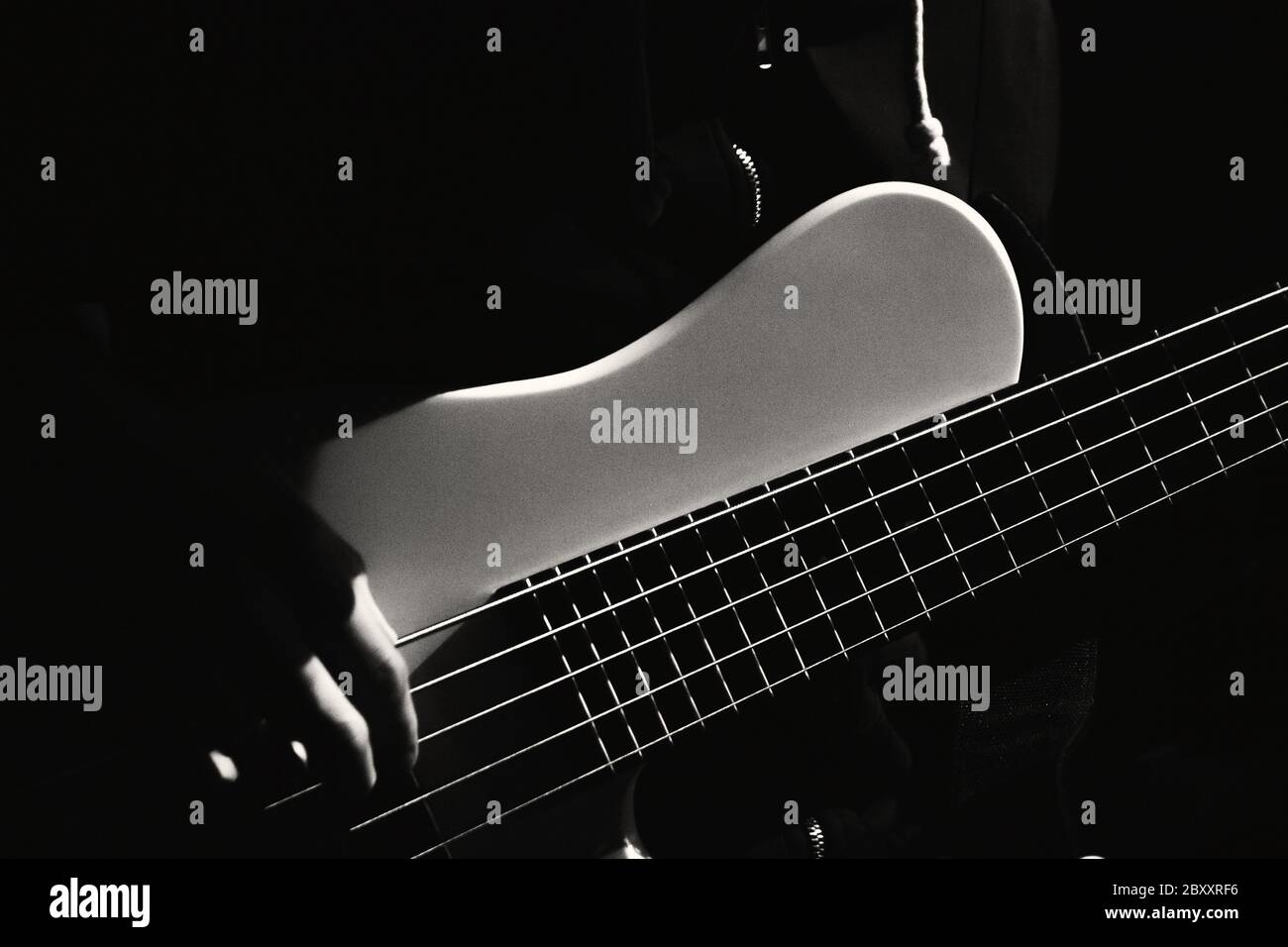 Close up view on five string bass guitar and fingers of musician lit by ...