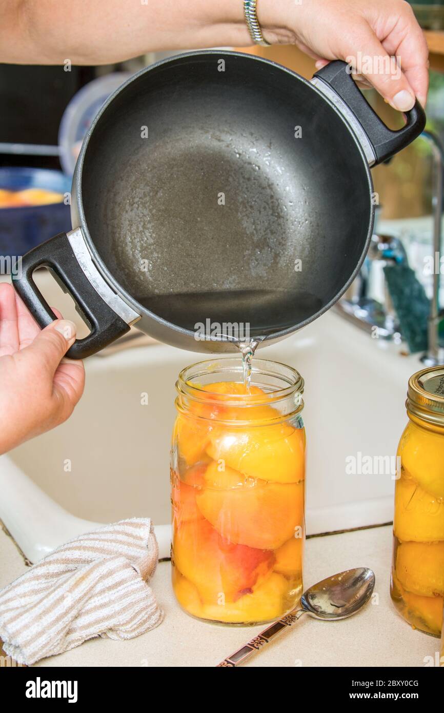 Pouring hot syrup mixture (sugar and water mixture) into a jar of peach ...