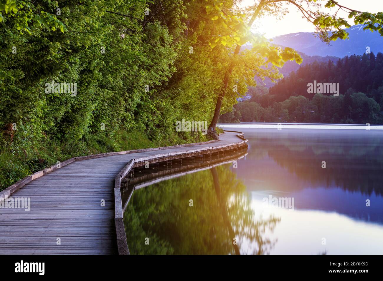 Wooden walkway around the lake Bled with mountains and houses on the ...