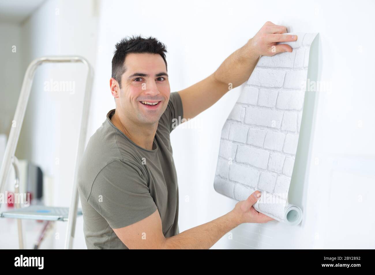 handyman putting up wallpaper on the white walls Stock Photo - Alamy