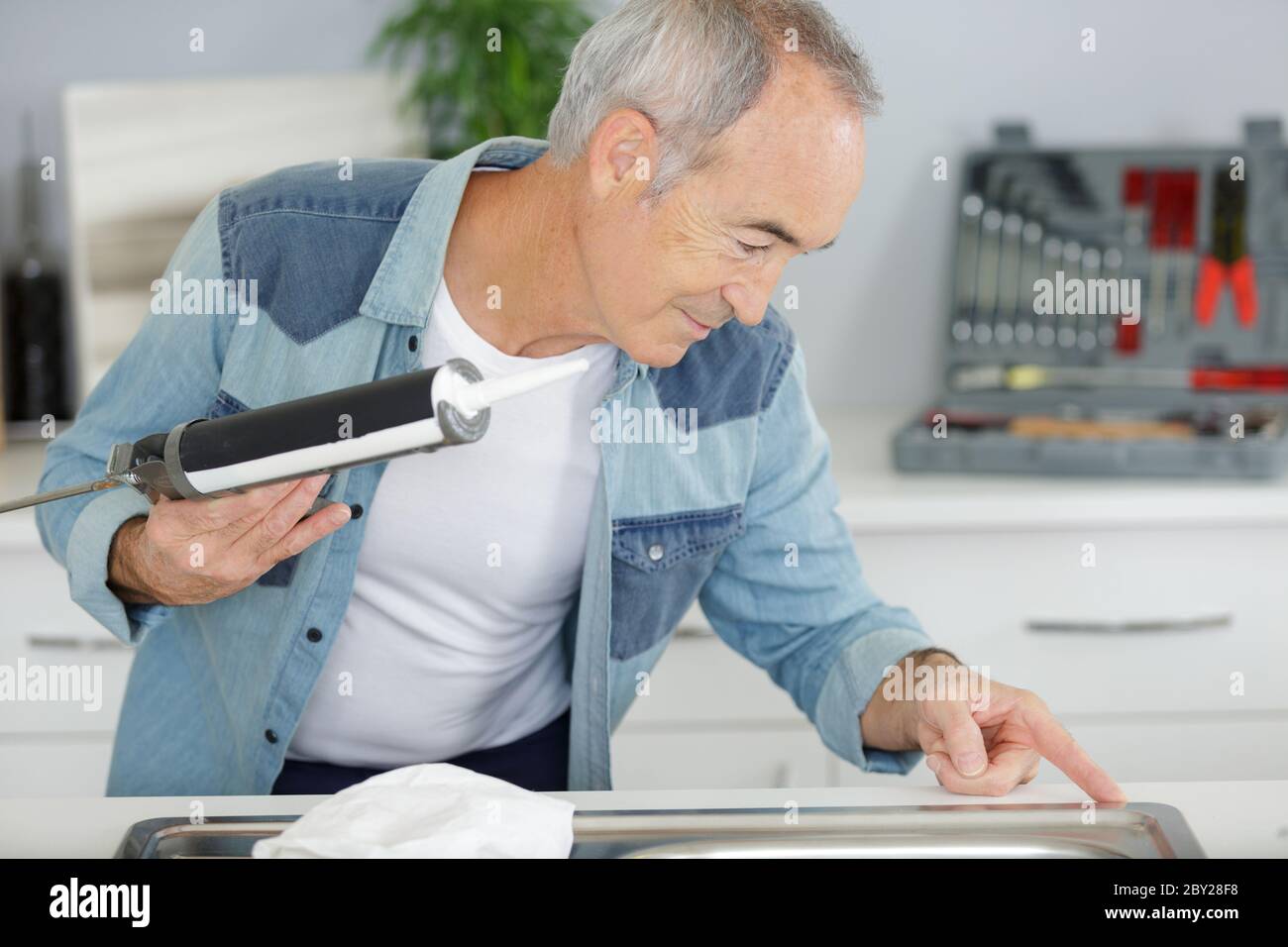 senior man using caulk gun around a sink Stock Photo - Alamy