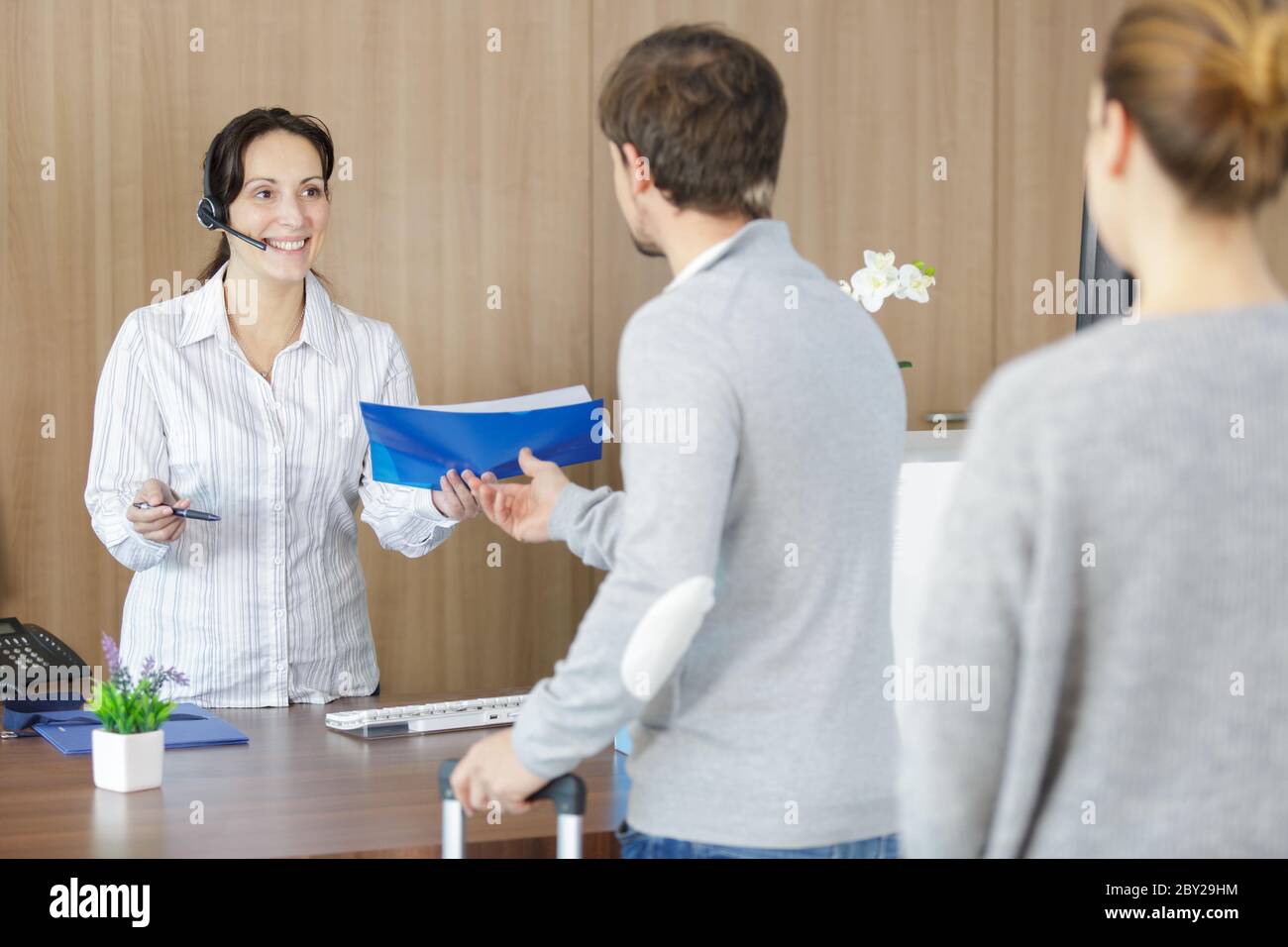 receptionist wearing headset passing file to man Stock Photo - Alamy