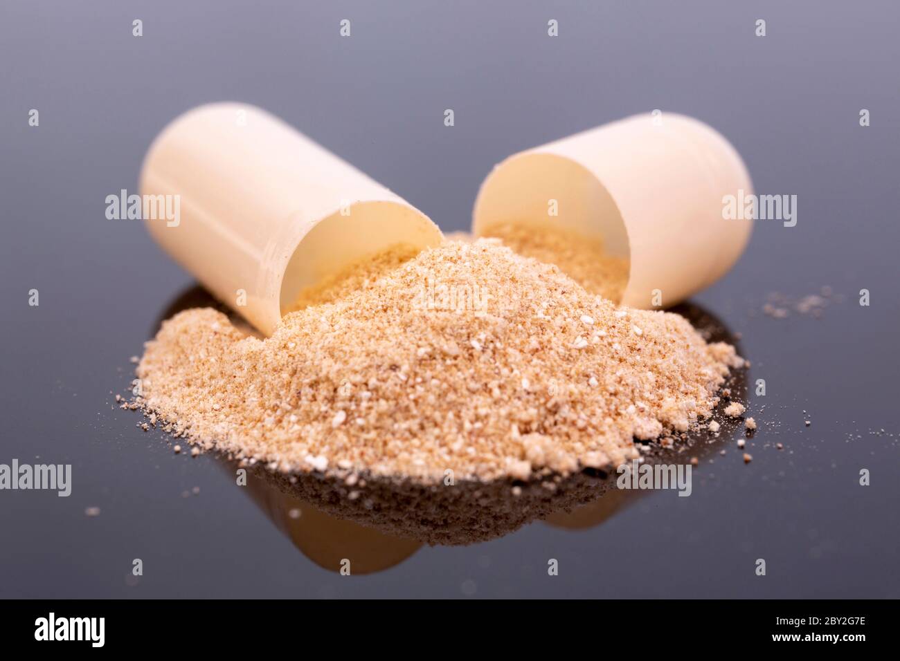 Single beige capsule and beige powder isolated on black reflective ...