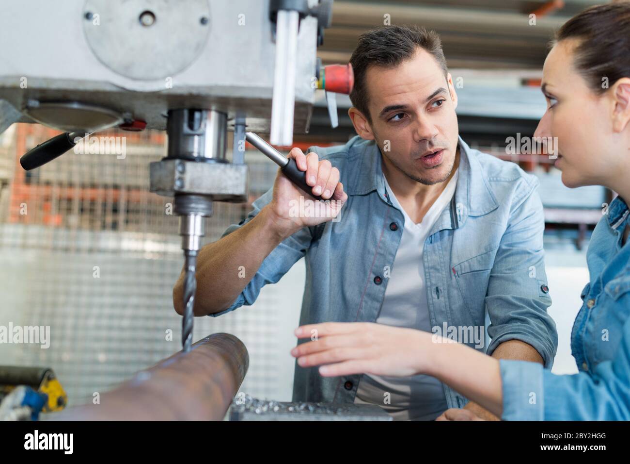 man showing woman how to use bench drill Stock Photo - Alamy