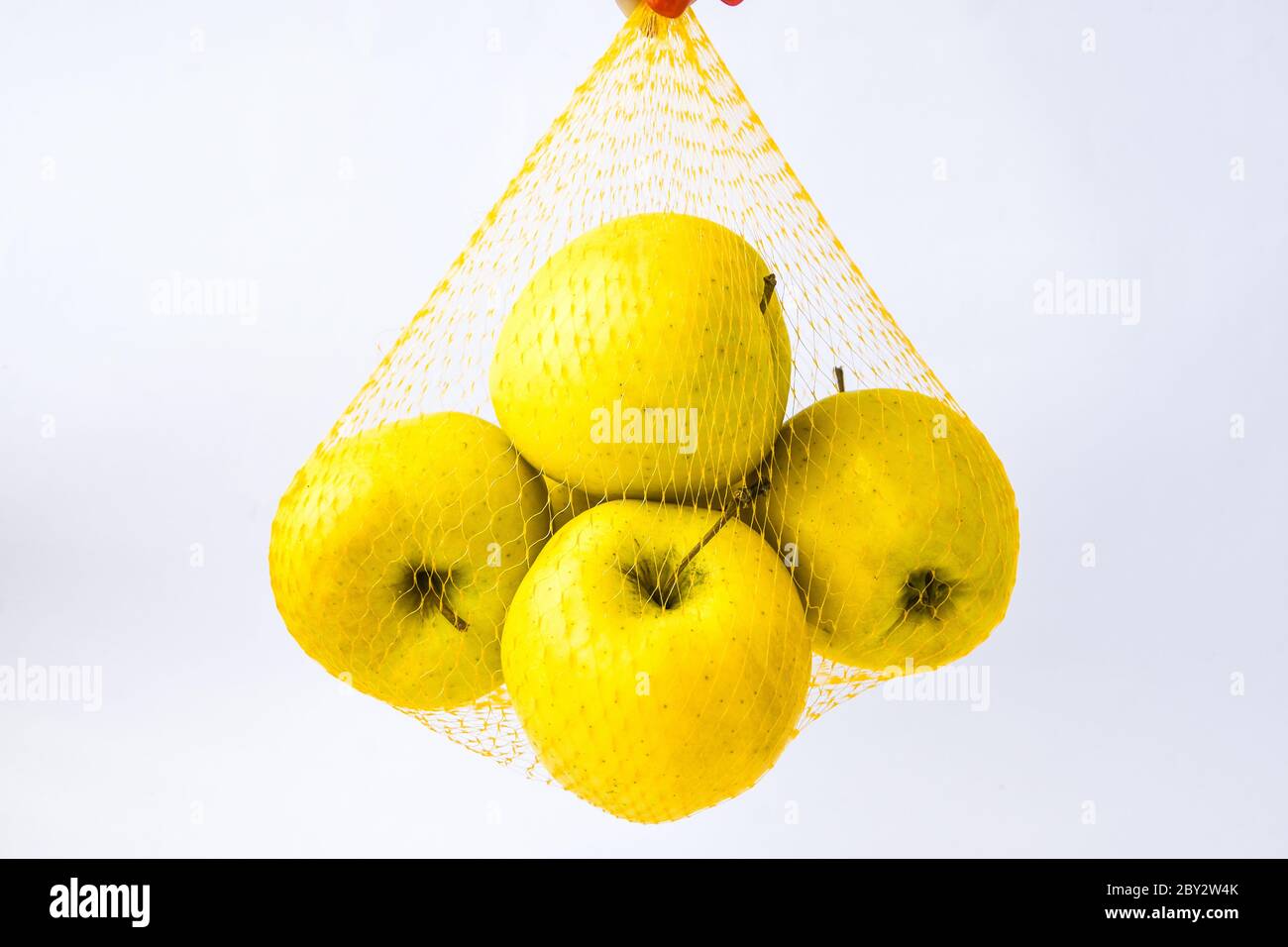 A group of apples in a orange mesh hanging in front of a white wall ...