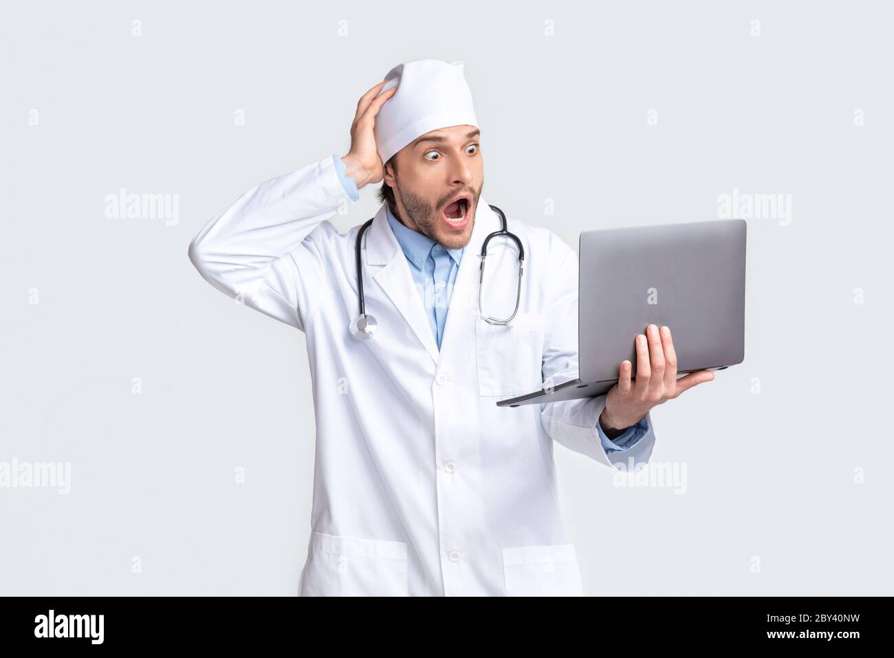 Shocked young doctor looking at laptop in amazement Stock Photo - Alamy