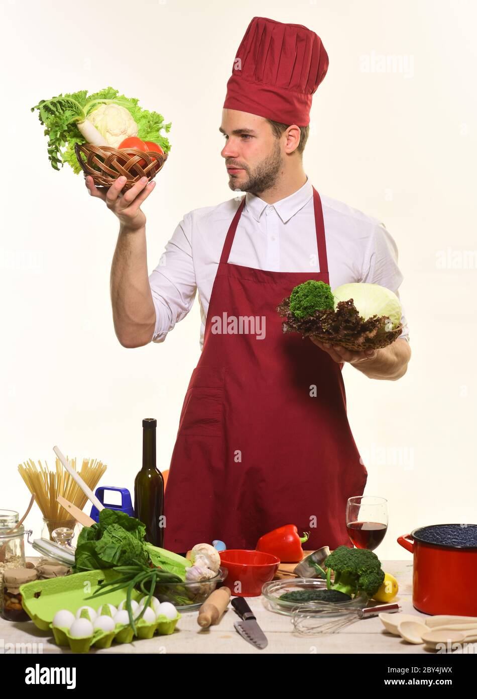 Cook stands by table with kitchenware and ingredients. Man with beard ...