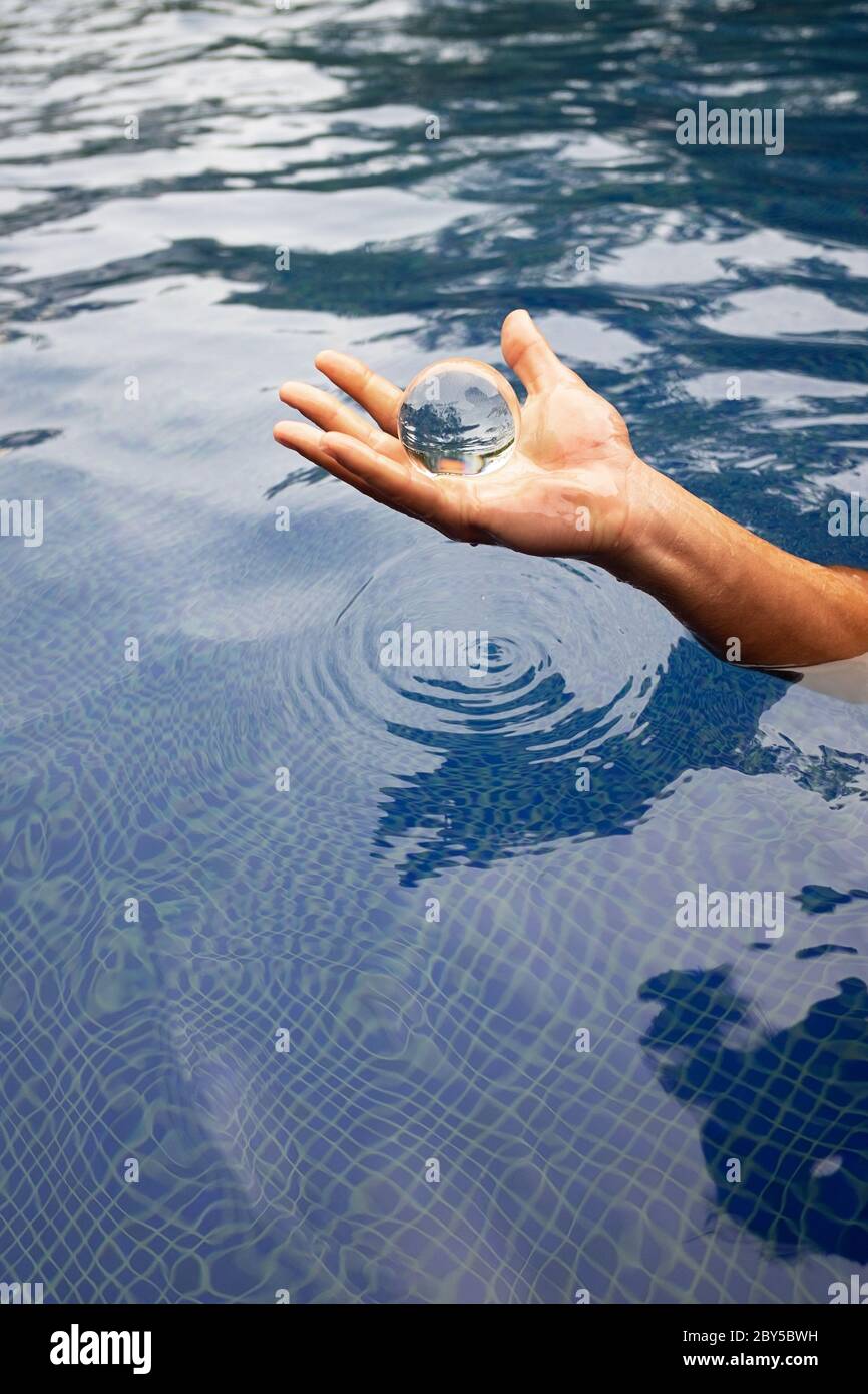 An Human hand holding a glass ball over the water Stock Photo - Alamy