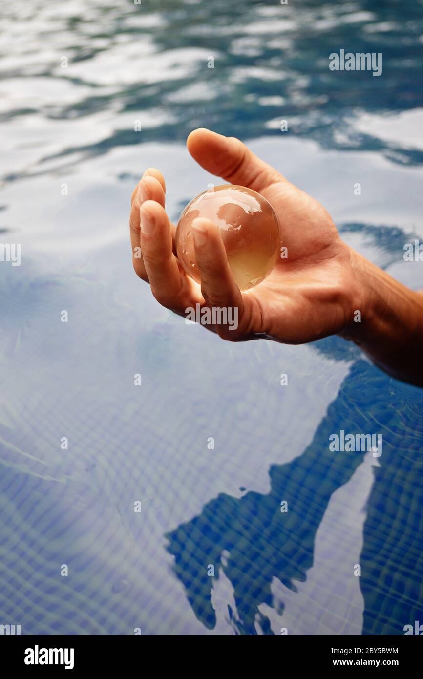 An Human hand holding a glass ball over the water Stock Photo - Alamy