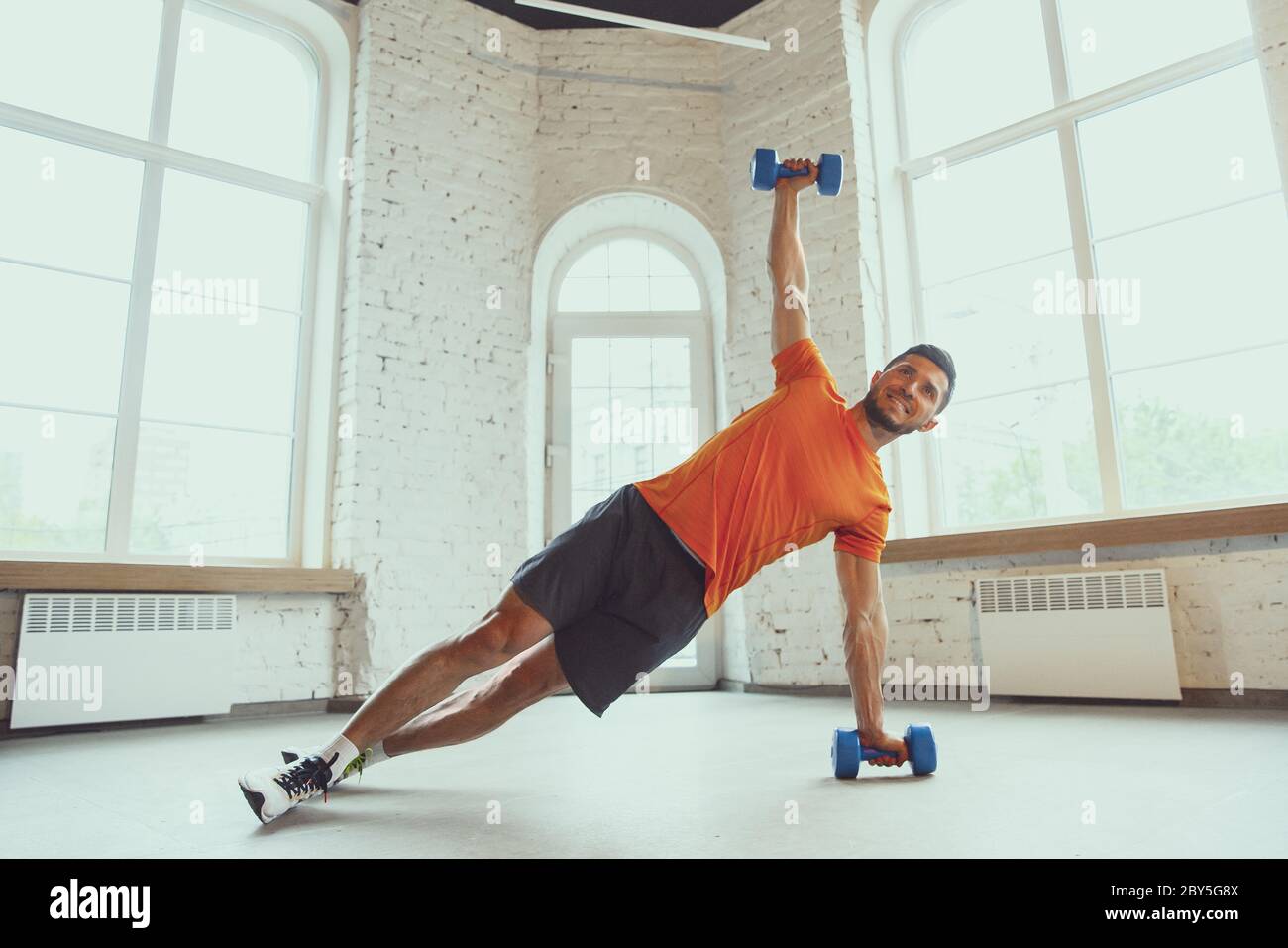 Dumbbell. Young caucasian man training at home during quarantine of ...