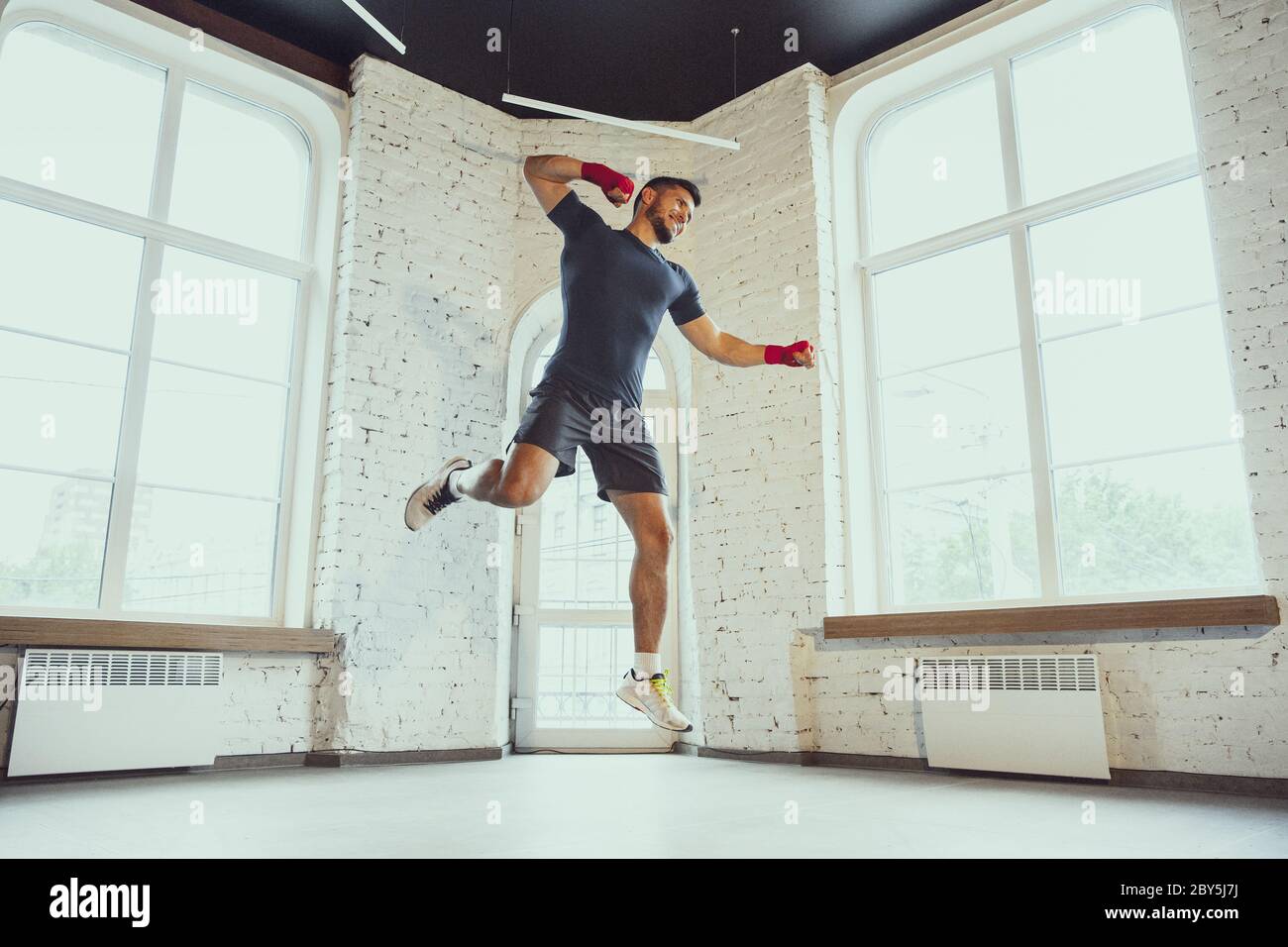 Kick in jump. Young caucasian man training at home during quarantine of ...