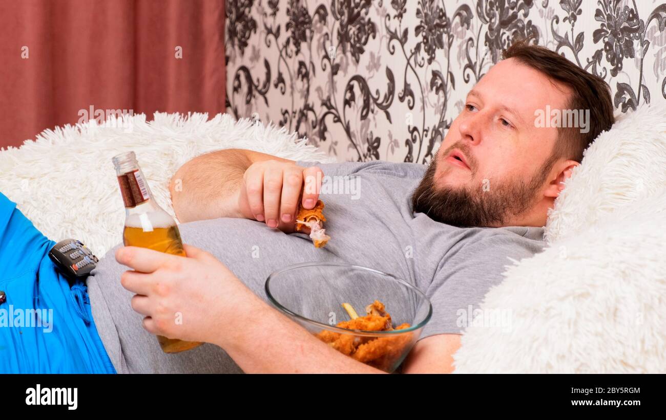 fat man drinks beer and eats unhealthy food chicken wings, bored in ...