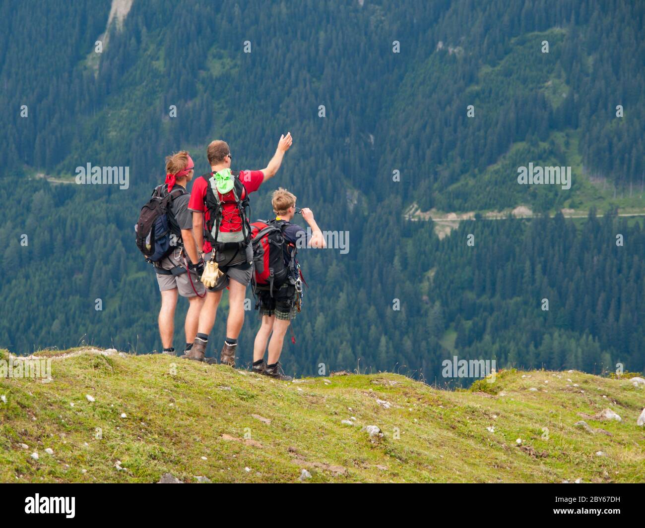 Three men looking around, discussing and pointing at mountains far away ...