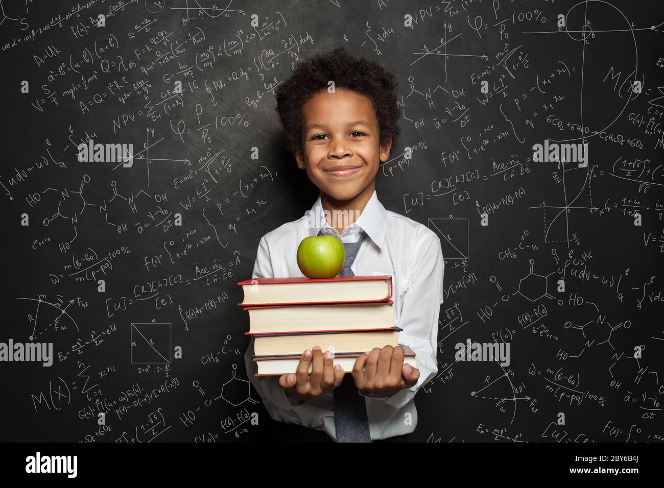 Smart black child student smiling and holding books and green apple ...