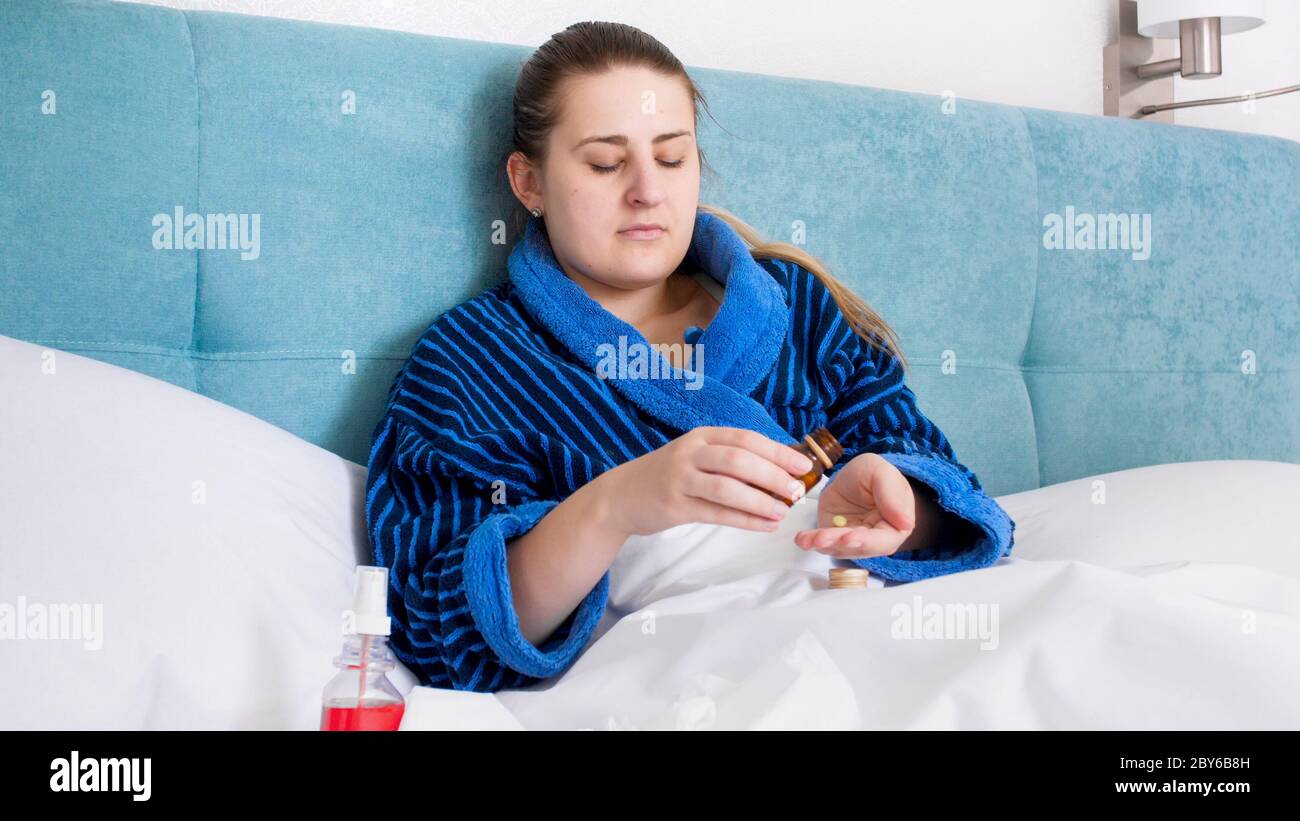Sick young woman lying in bed and holding pills on hand Stock Photo - Alamy