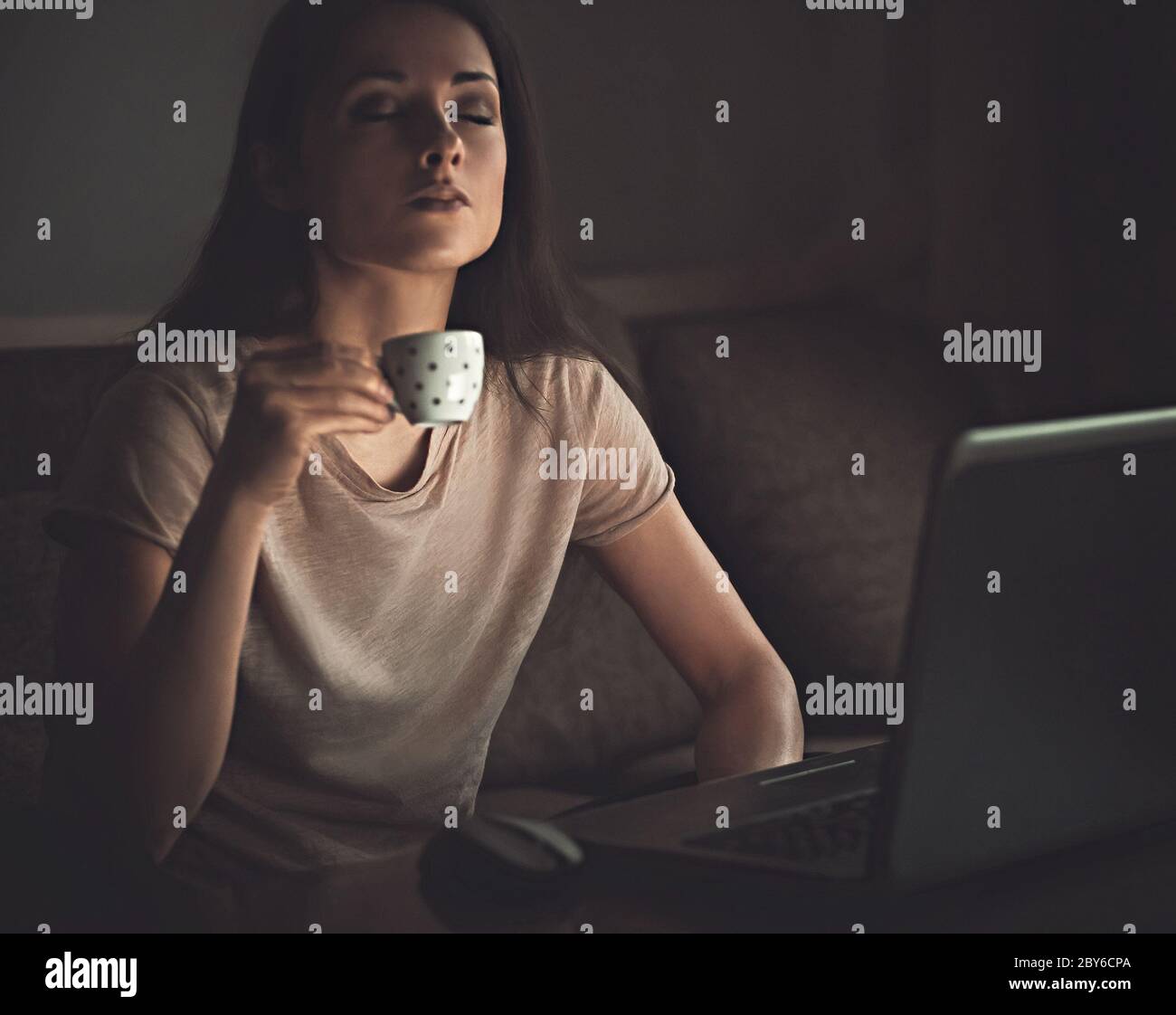 Beautiful woman sitting near the computer monitor and enjoying drinking ...