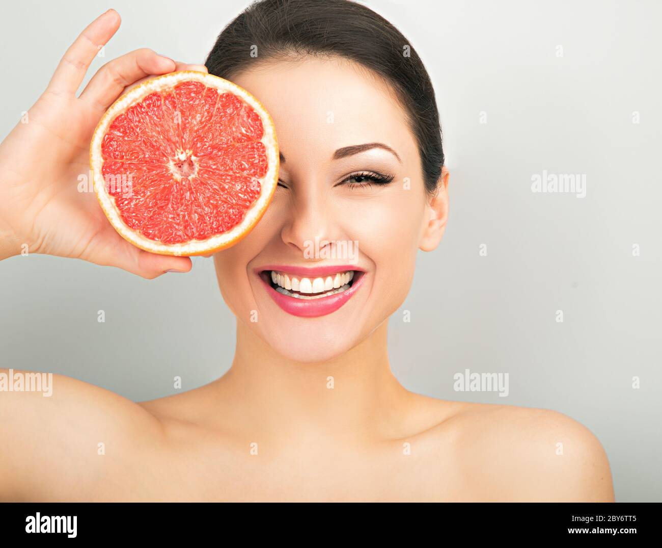 Happy smiling clean skin woman holding red grapefruit near the face ...