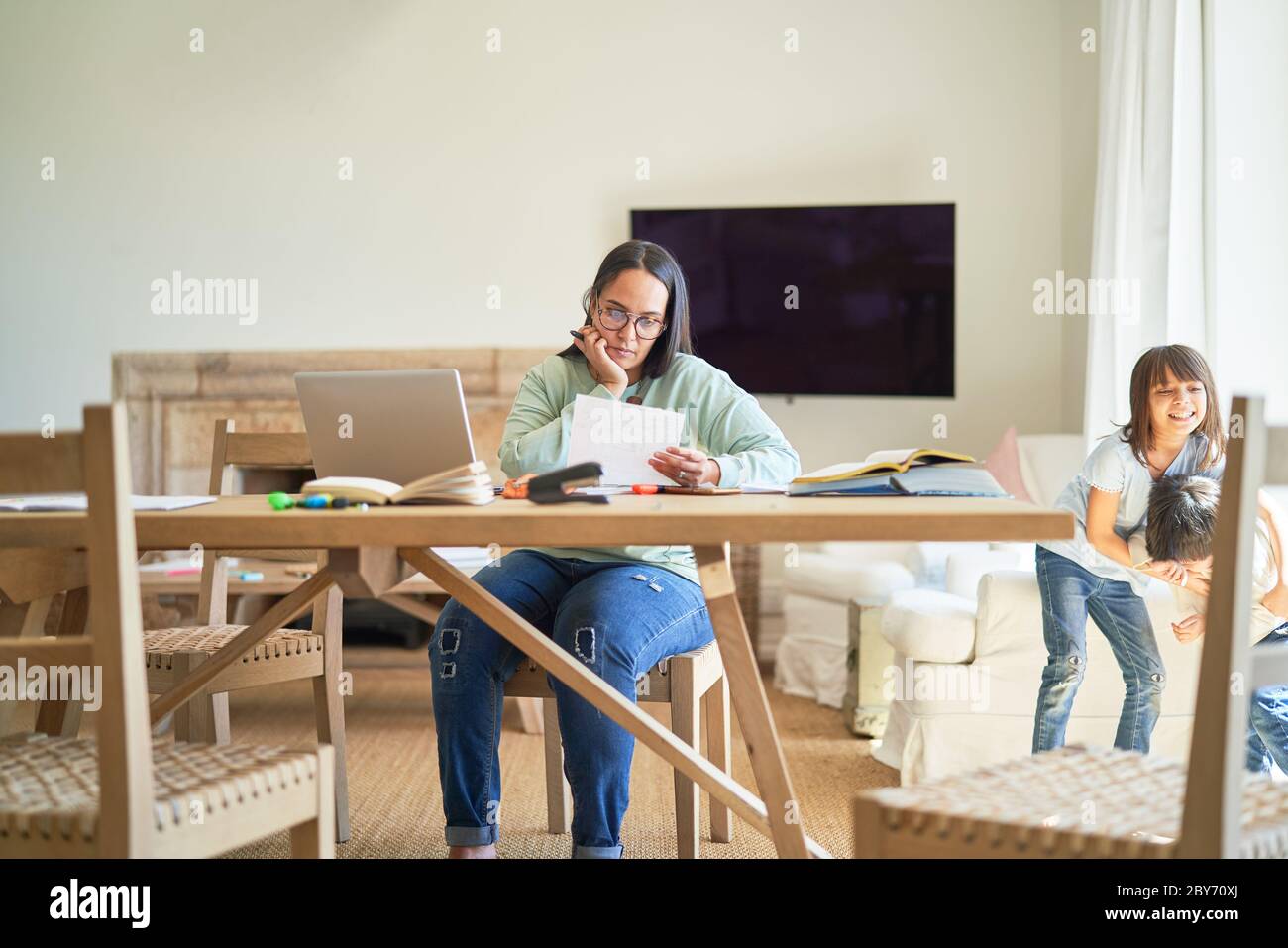 Kids playing next to mother working at table Stock Photo - Alamy
